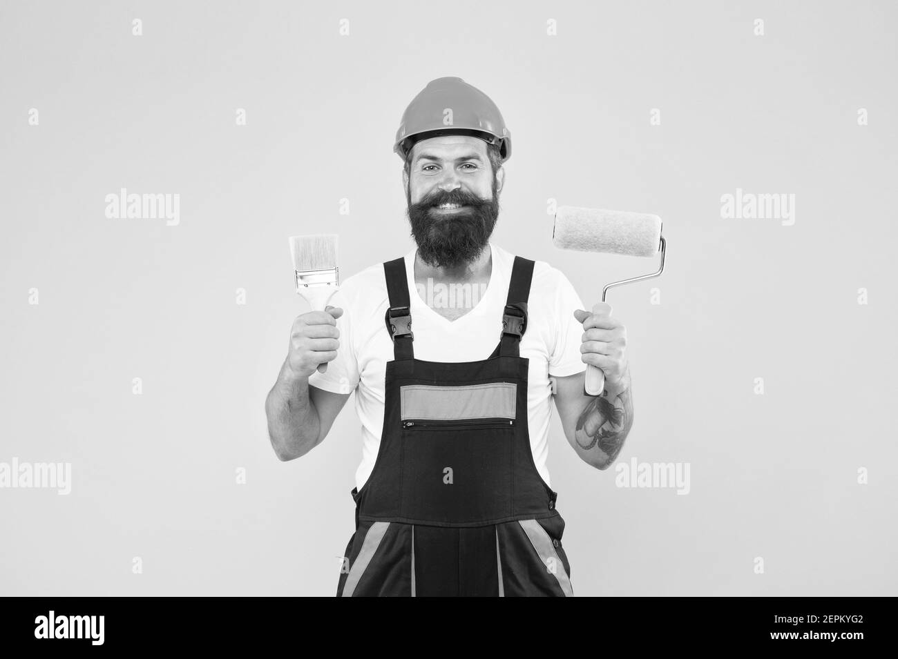 Happy bearded man in hard hat and working uniform hold paint roller and ...