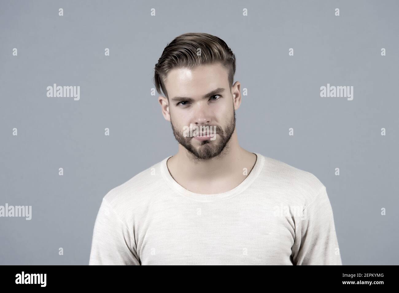 Man with unshaven face hair and fashionable haircut in white shirt pose ...