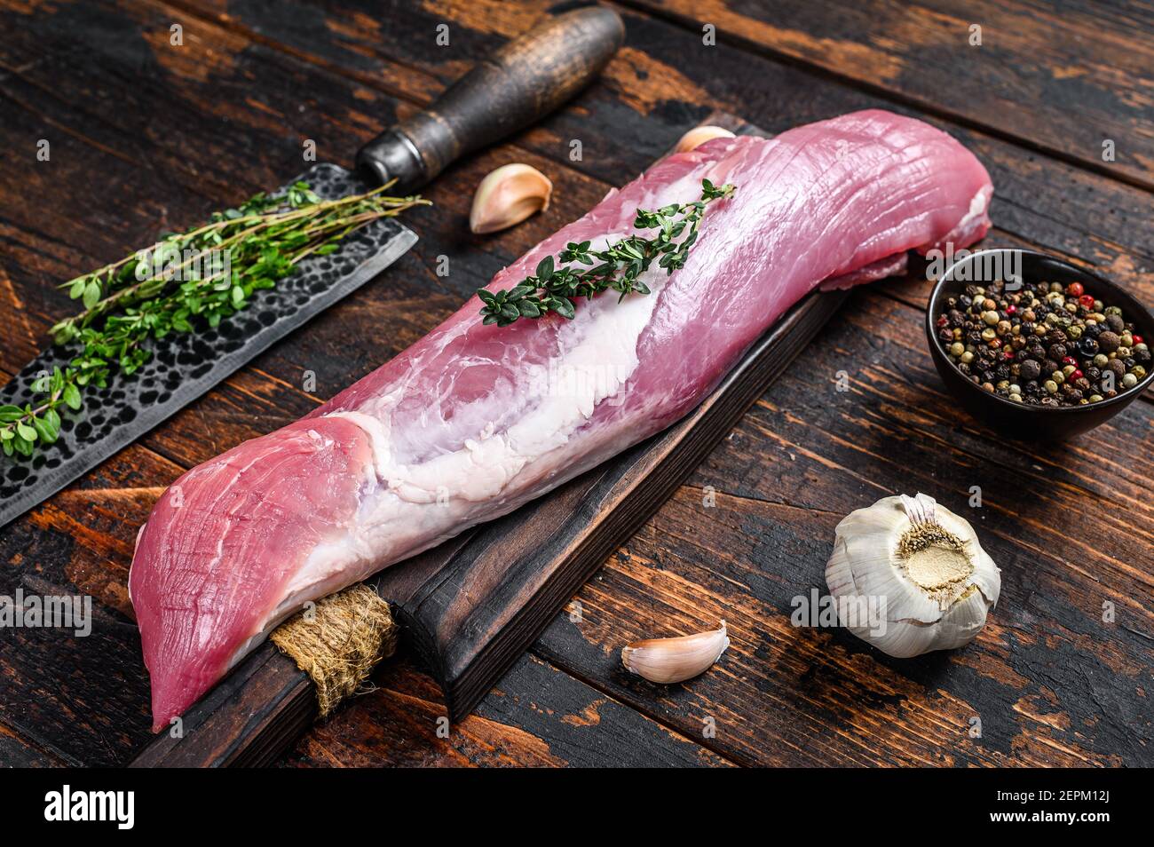 Raw fresh pork tenderloin meat on a cuuting board with cleaver. Dark ...
