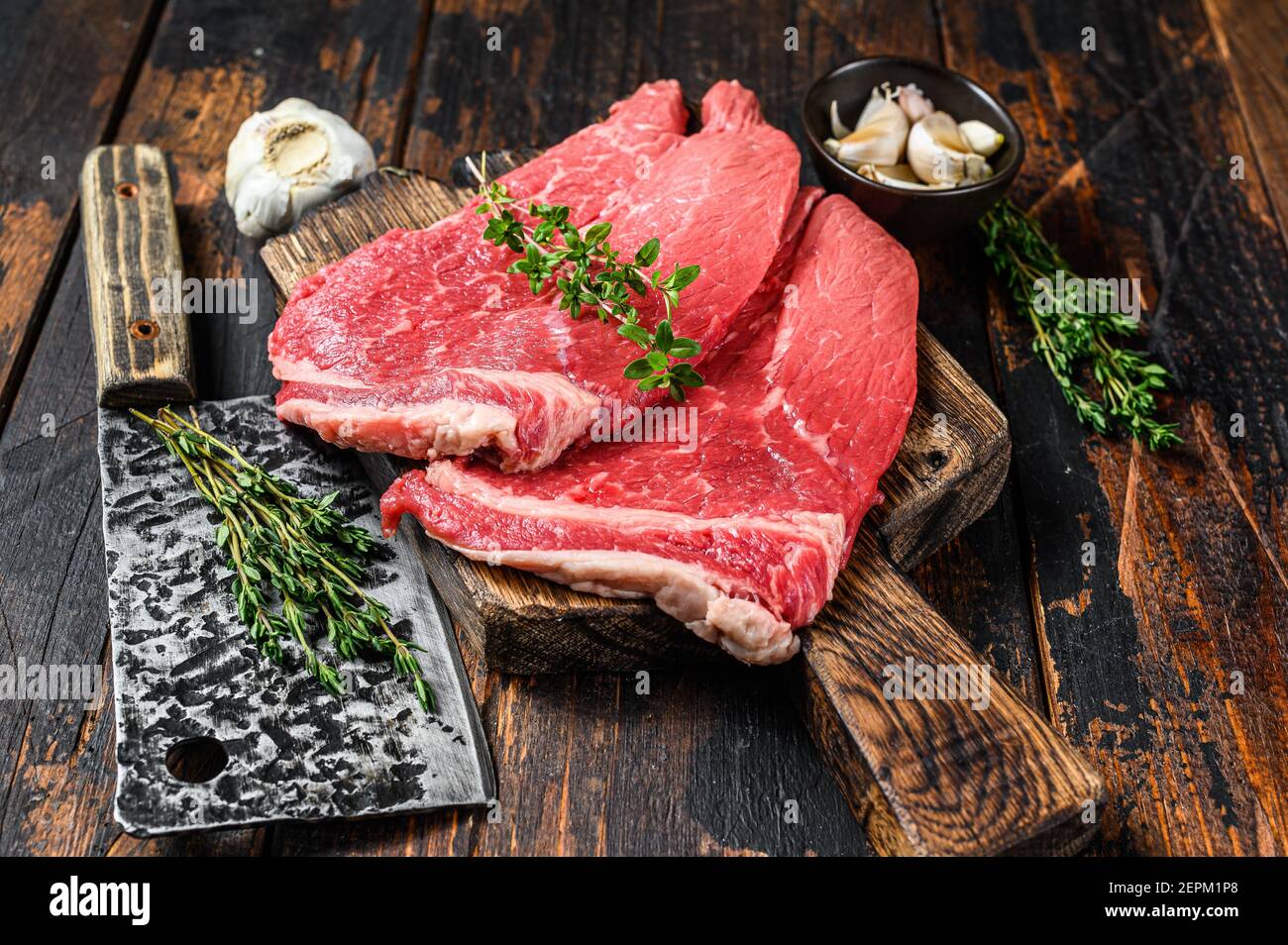 Raw beef meat chop rump steak on a cutting board. Dark wooden ...