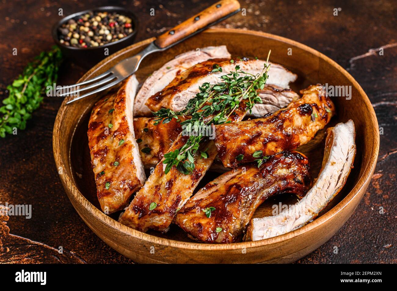 Cut BBQ grilled pork rack spareribs in a wooden plate. Dark background ...