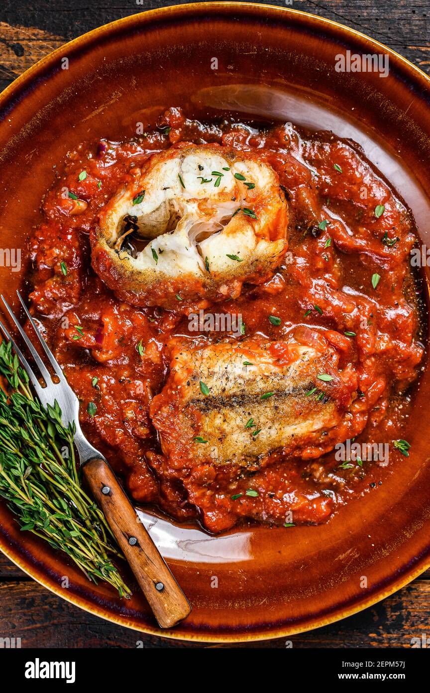 Roast grenadier white fish fillet with tomato sauce in a plate. Dark ...