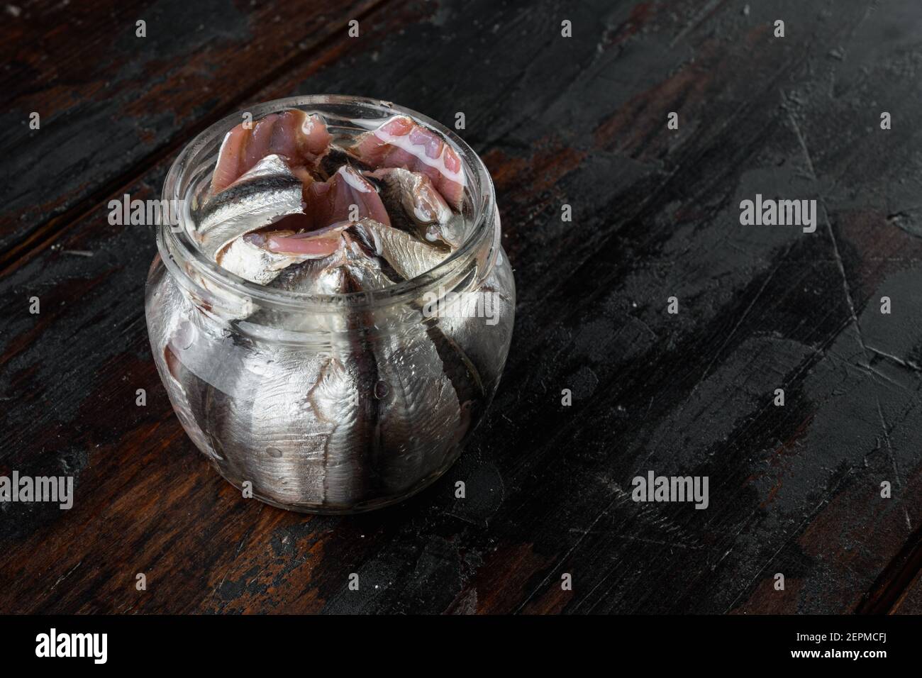 Salted anchovy fillets set, in glass jar, on old dark wooden table ...