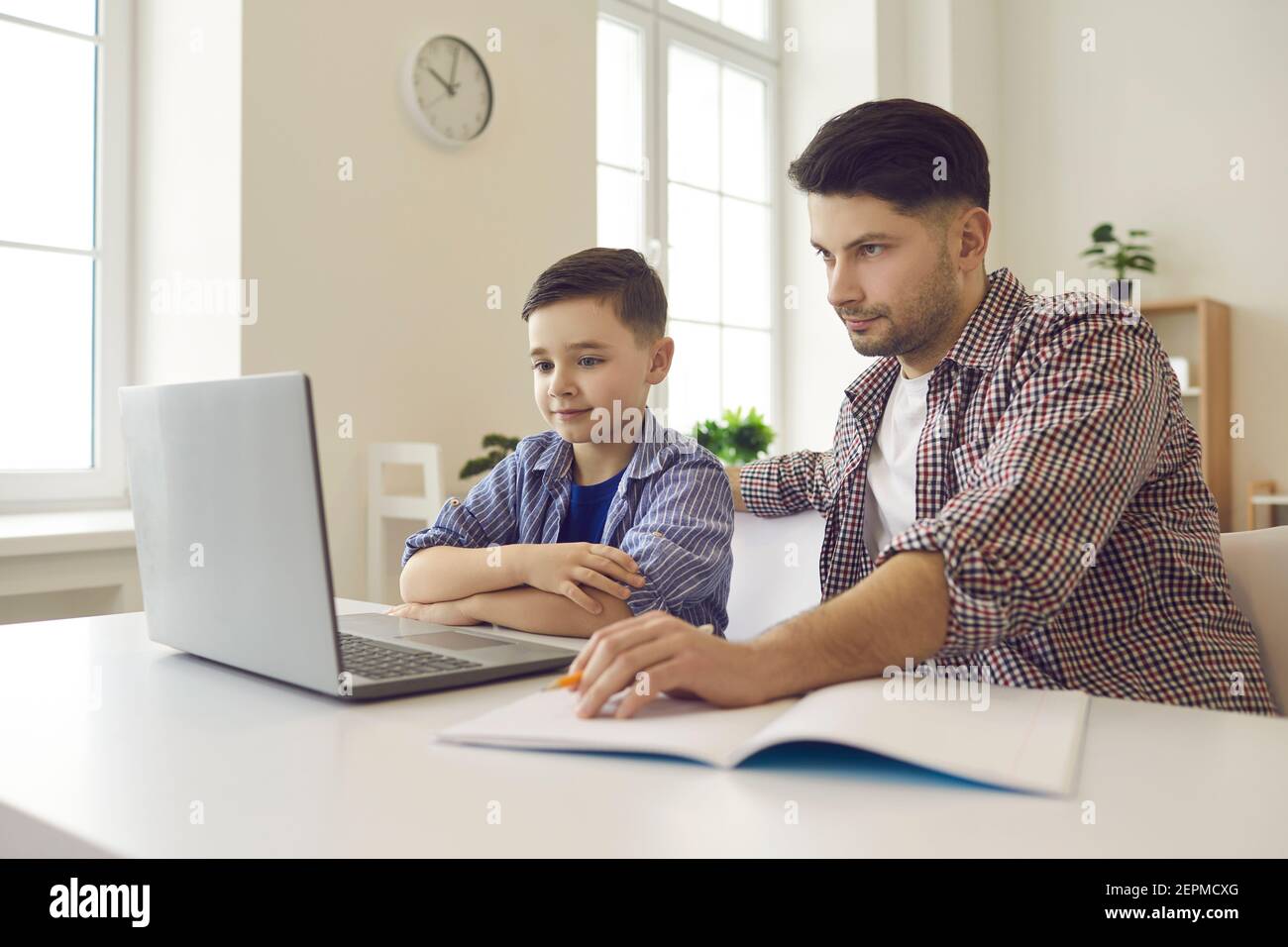 Dad sits with his son and helps him with his studies using a laptop to ...