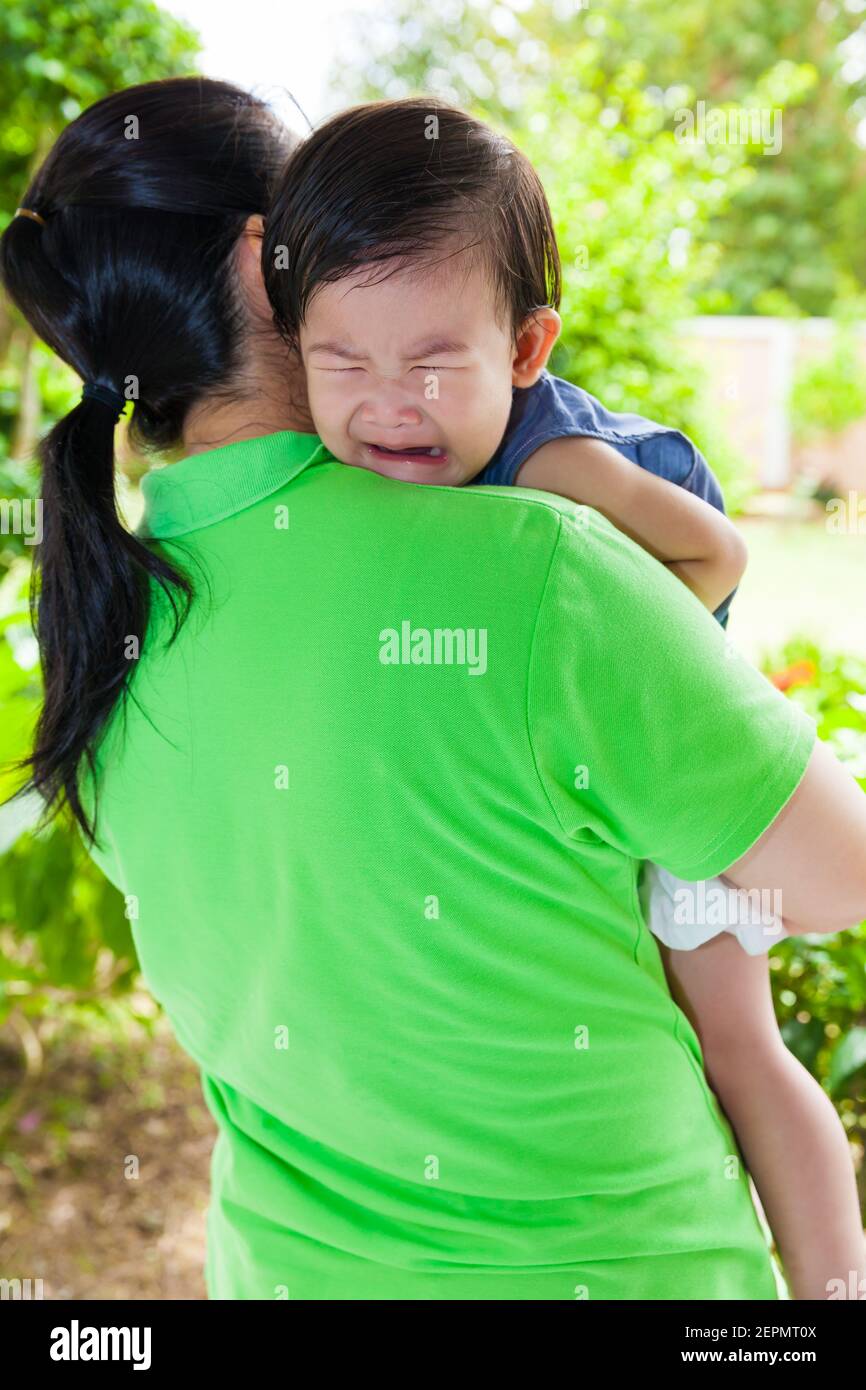 Mother Carrying And Comfort Her Daughter In Backyard Over Blur Green
