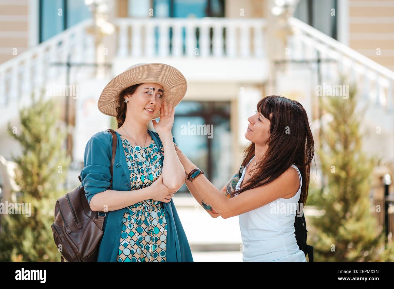 Two young women are chatting in the street. One woman listens with ...