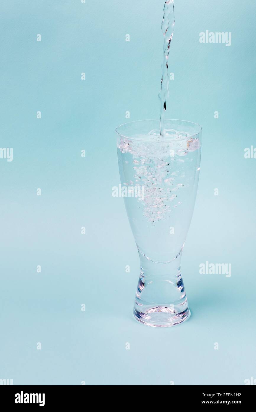 A jet of water fills transparent glass against a blue background. White ...
