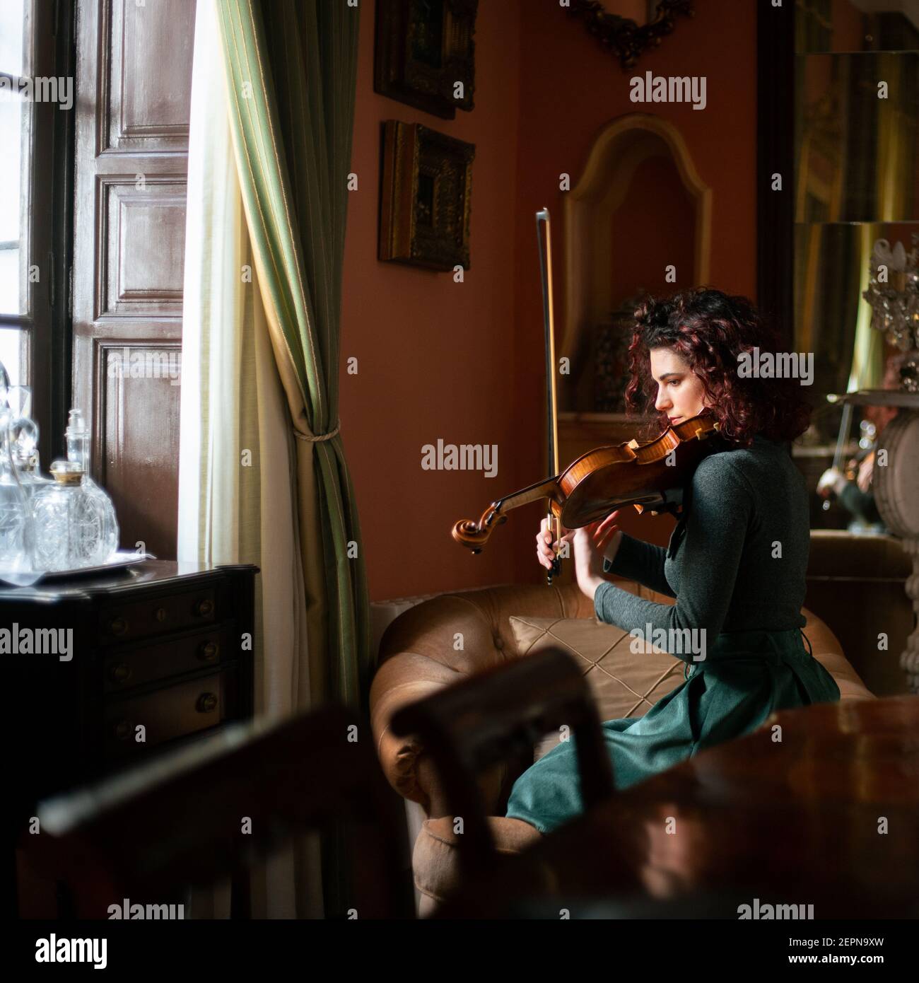Side view of skilled female musician playing violin while sitting on ...