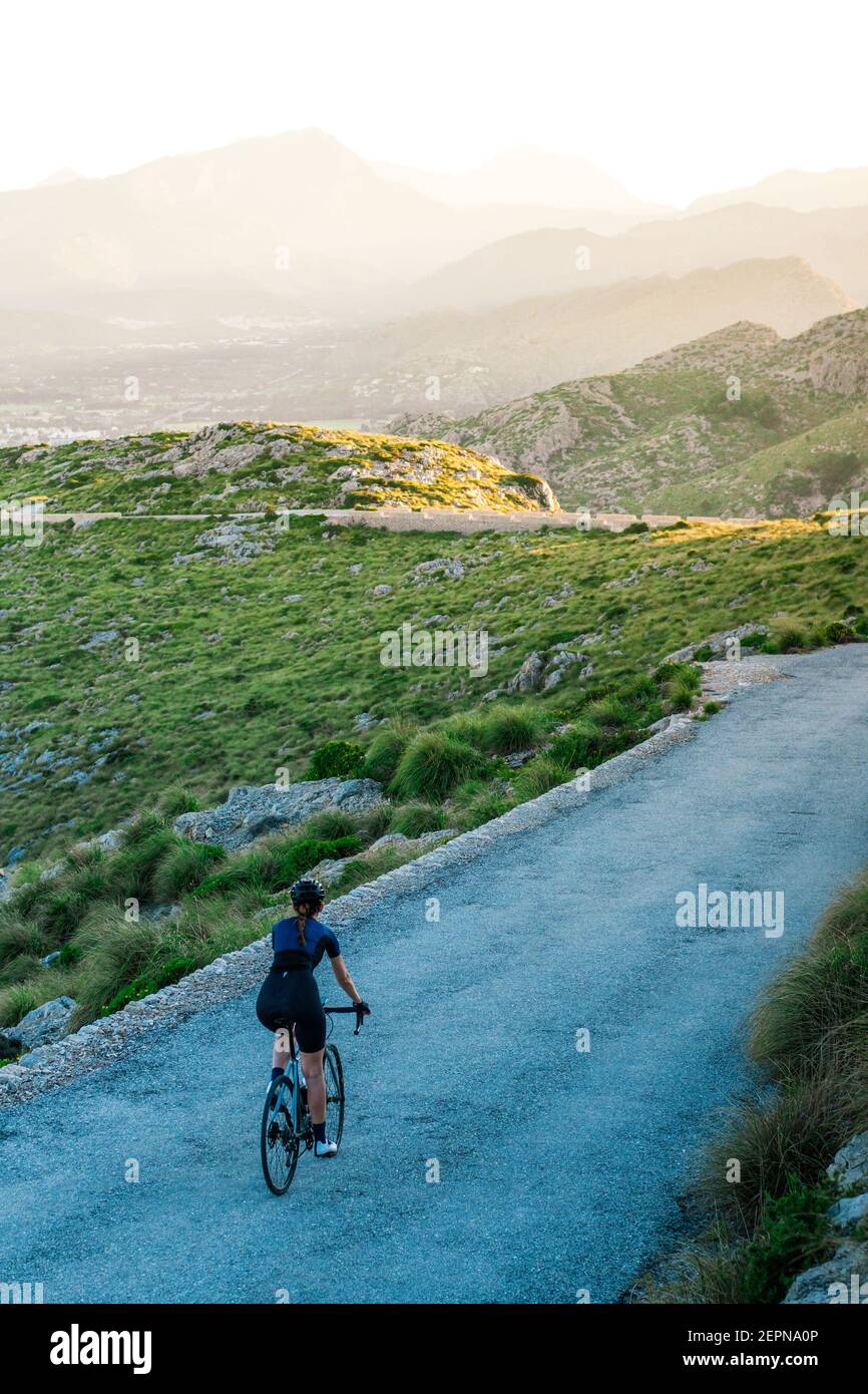Back view of anonymous female cyclist in casual outfit riding bicycle ...