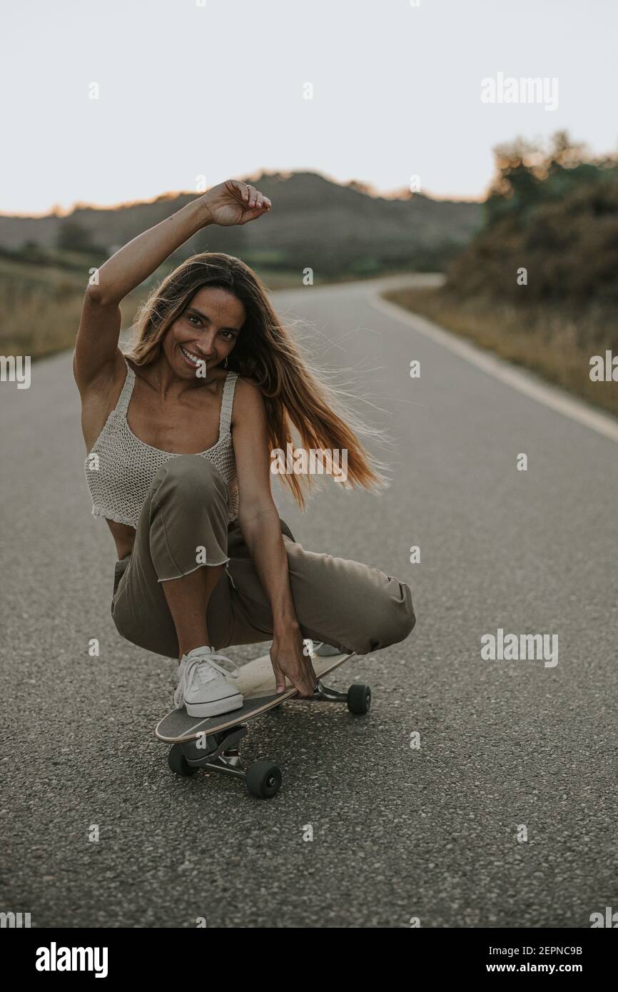 Full body attractive carefree female skater sitting on haunches on ...