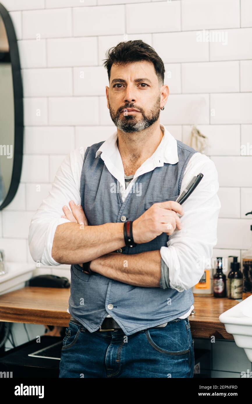 Masculine male stylist holding straight razor with sharp blade while ...