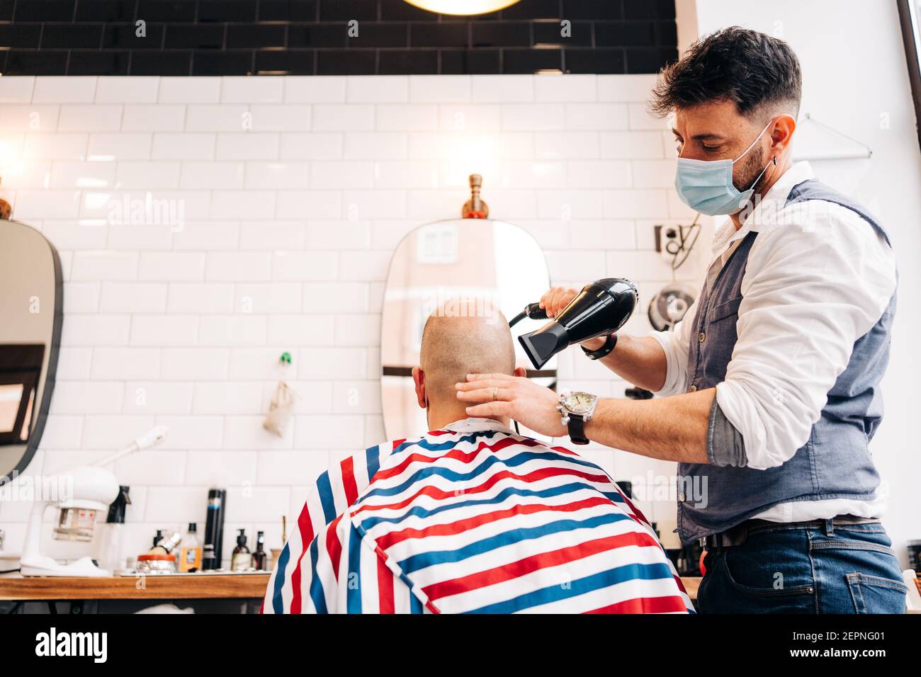 Anonymous male stylist in mask using hairdryer while touching bald head ...