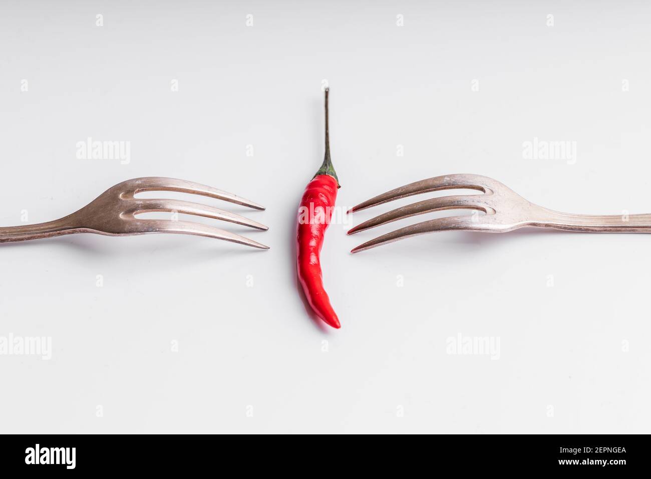 From above of arranged red hot chili peppers with forks on white ...
