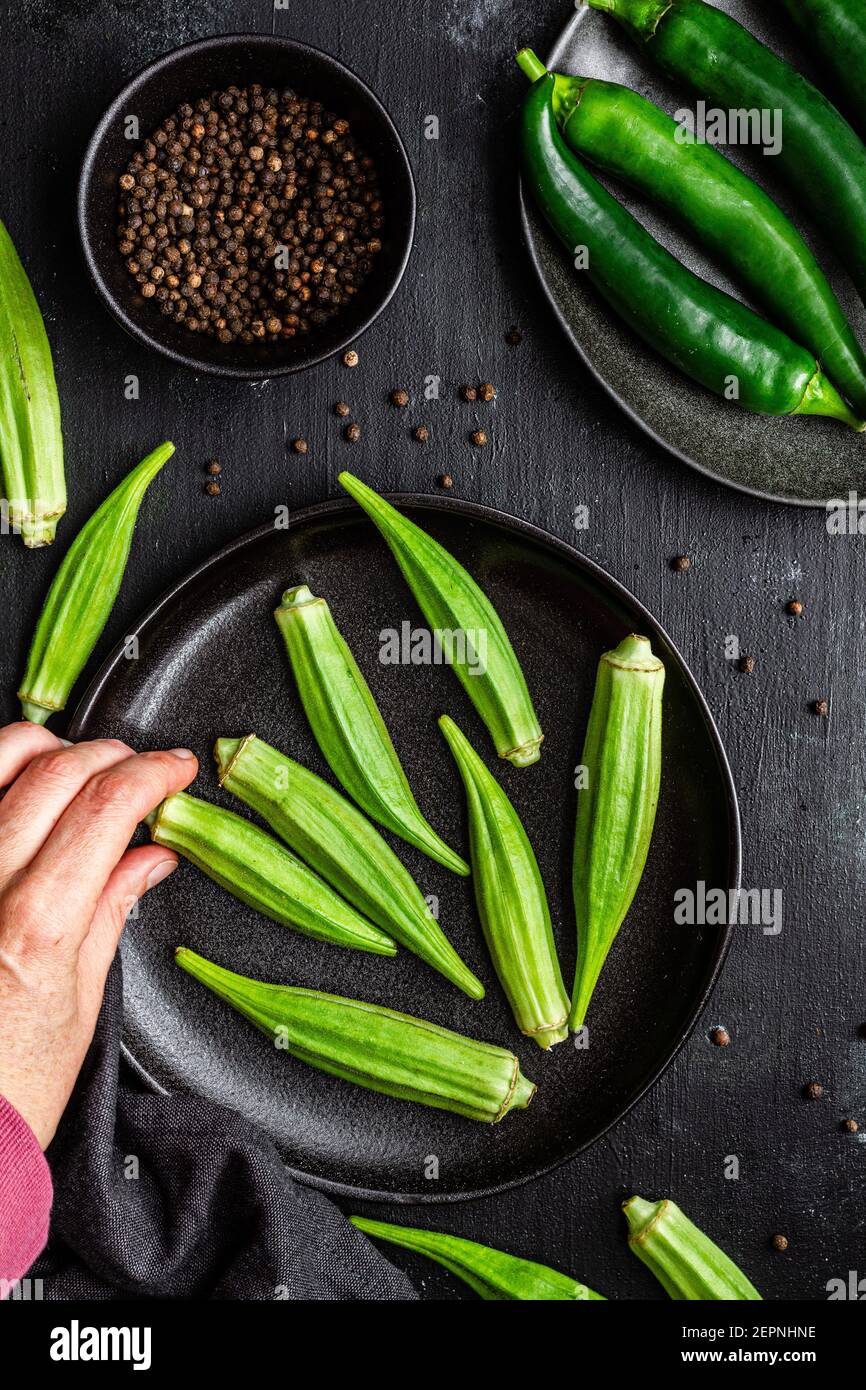 Crop unrecognizable person holding ripe okra over table with fresh ...