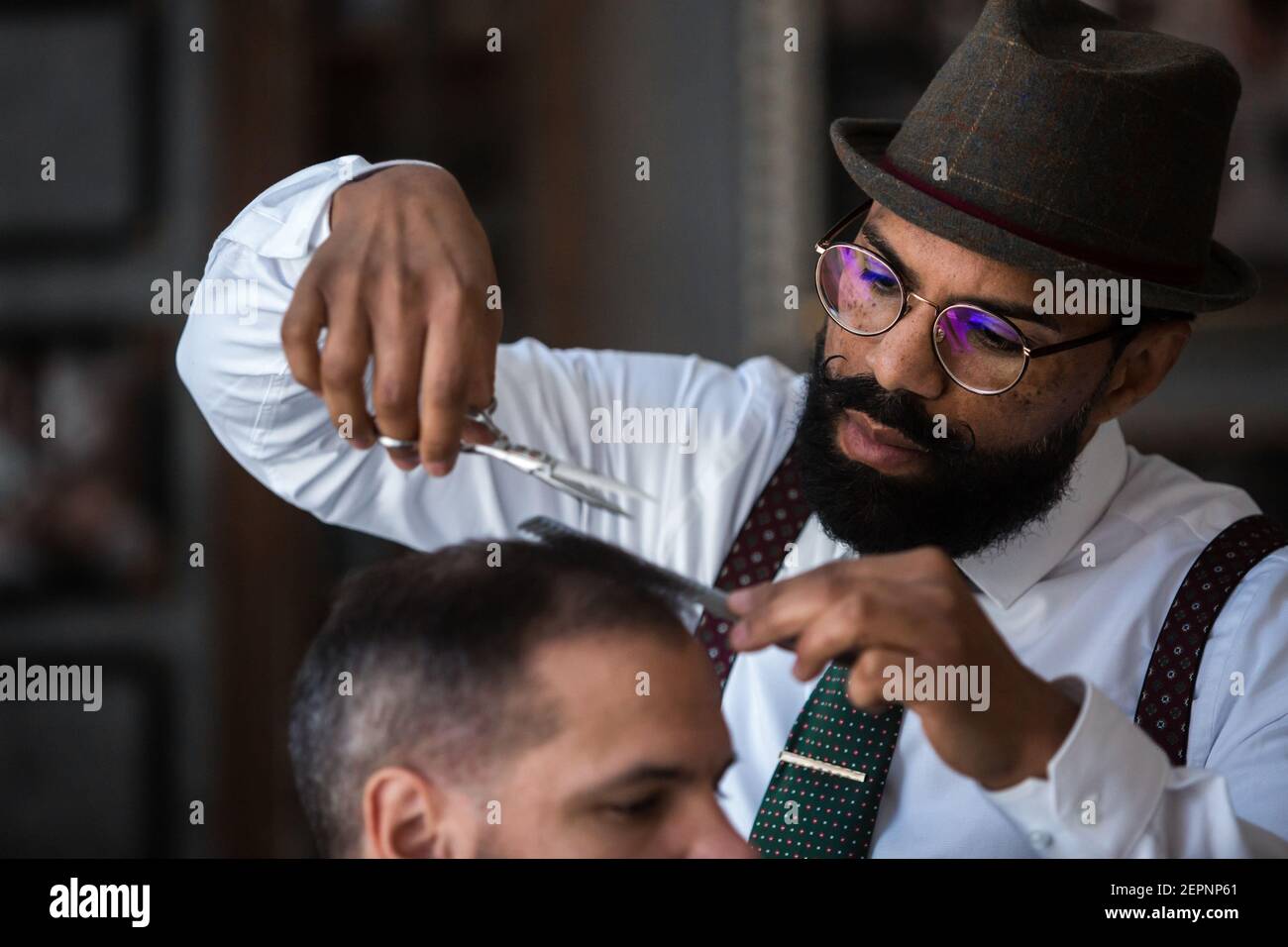 Serious mature bearded ethnic male barber trimming hair of client with ...
