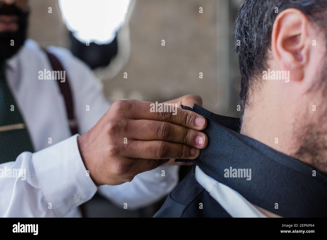 Cropped unrecognizable ethnic male beauty master putting on cape ...