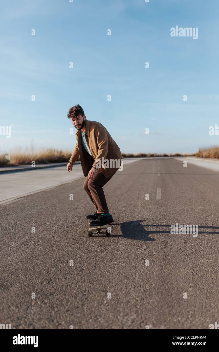 Full body young bearded male skater in stylish wear riding skateboard ...
