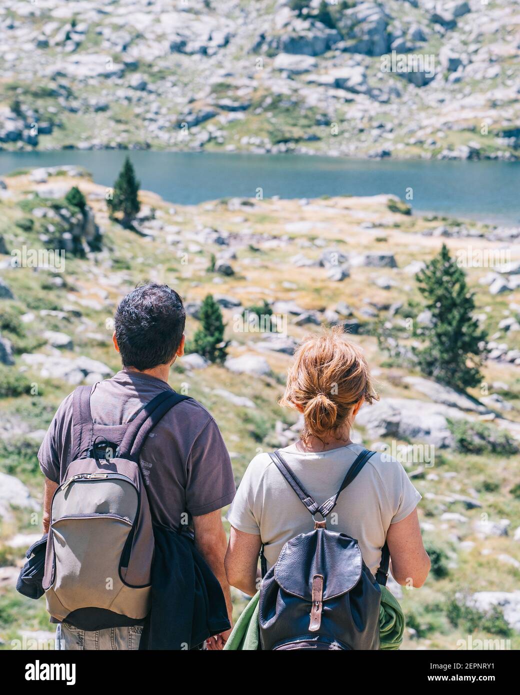 Back view of anonymous backpackers contemplating lake between mounts ...