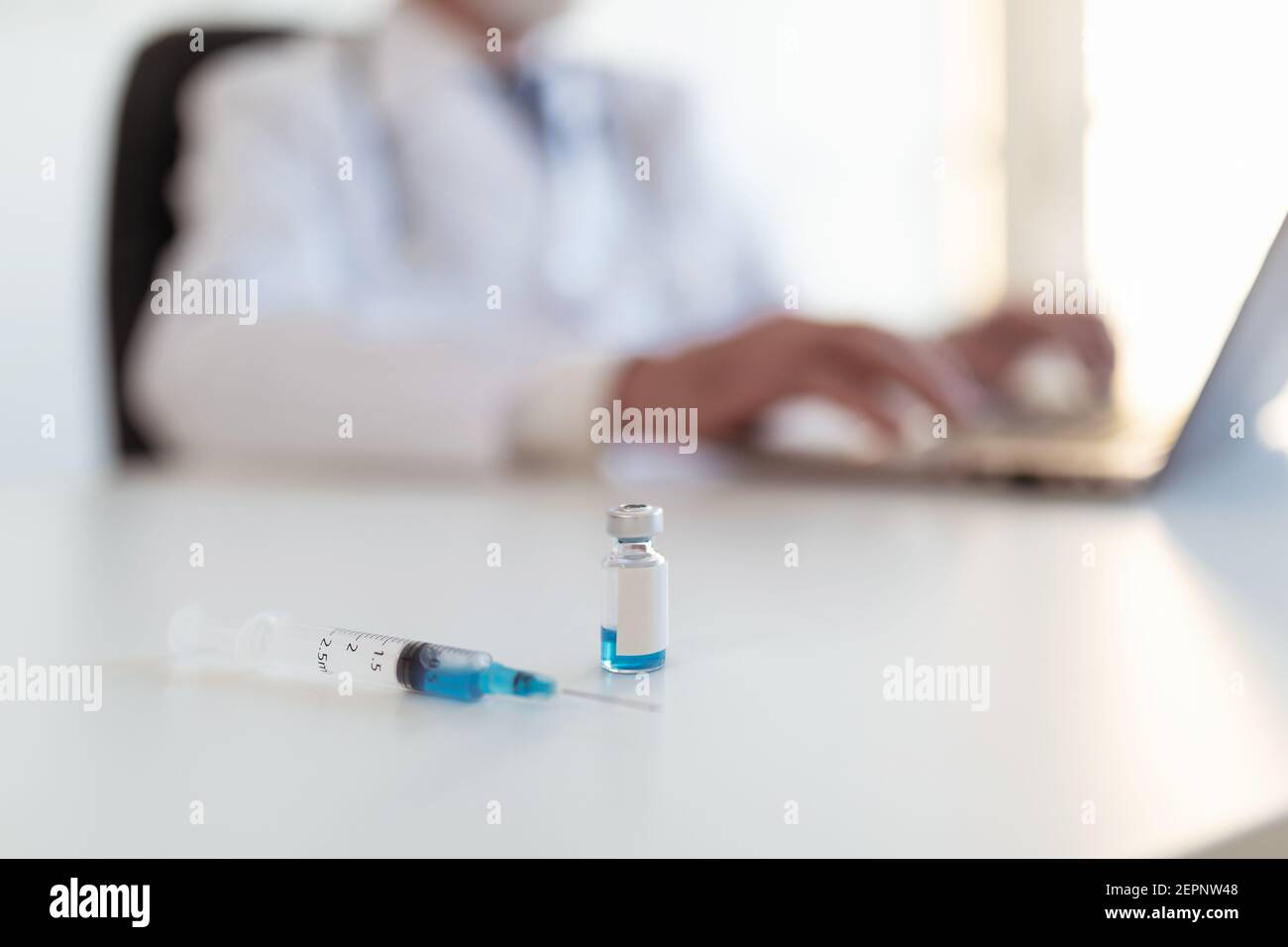 Crop anonymous doctor working on netbook on table with injector and ...