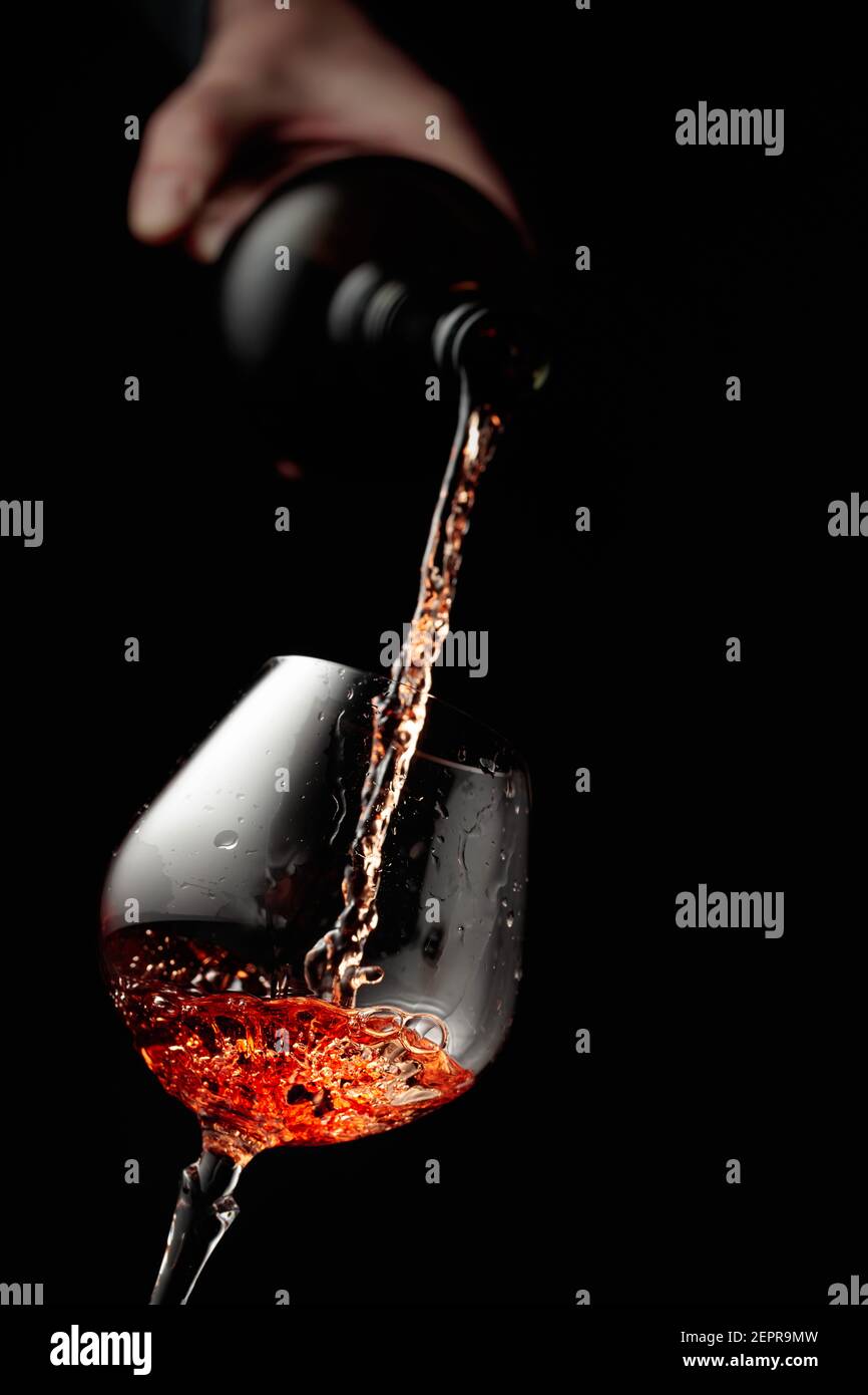 Pouring brandy in a glass goblet. Black background with copy space ...