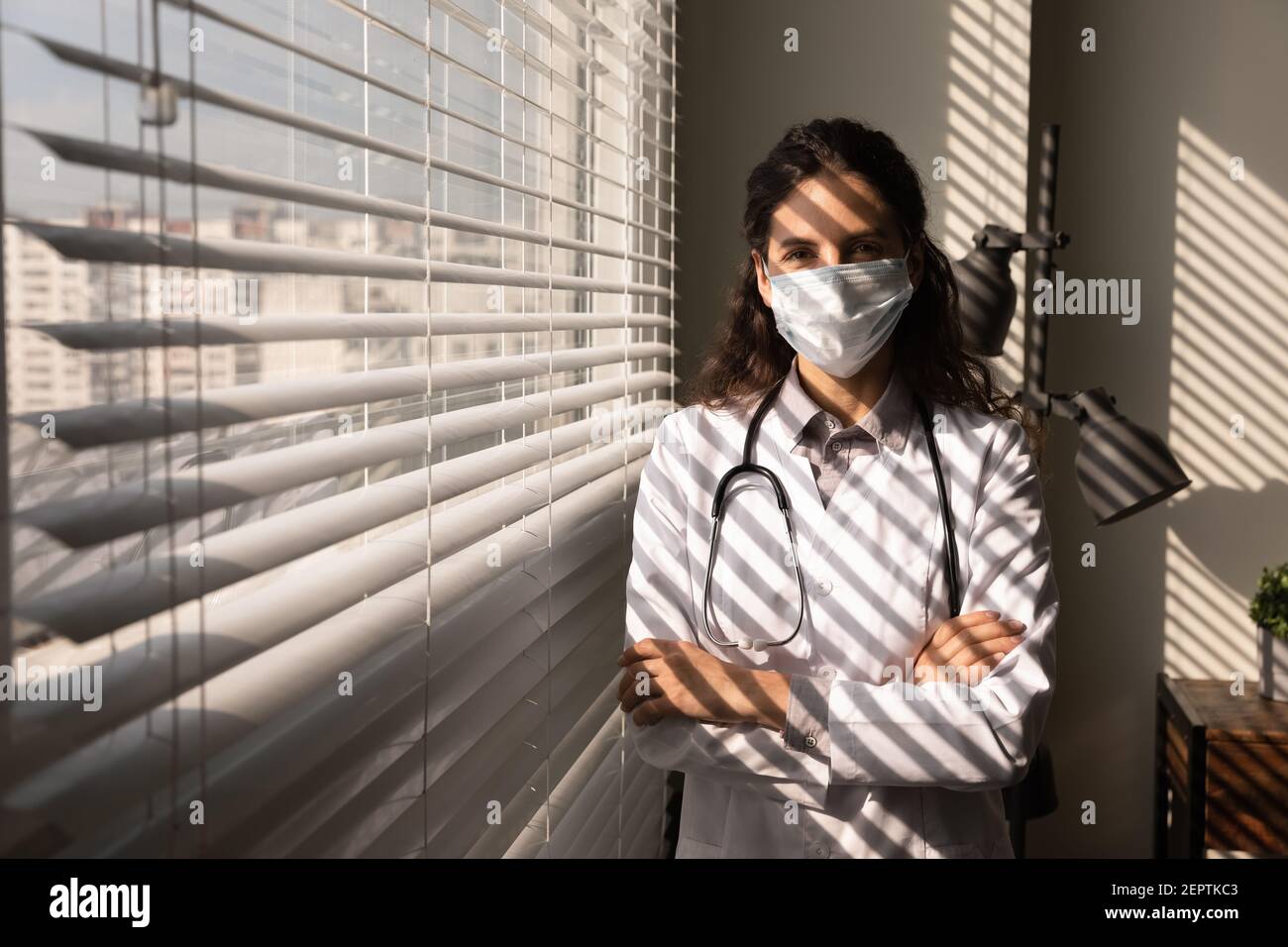 Portrait confident female doctor wearing mask standing near window ...