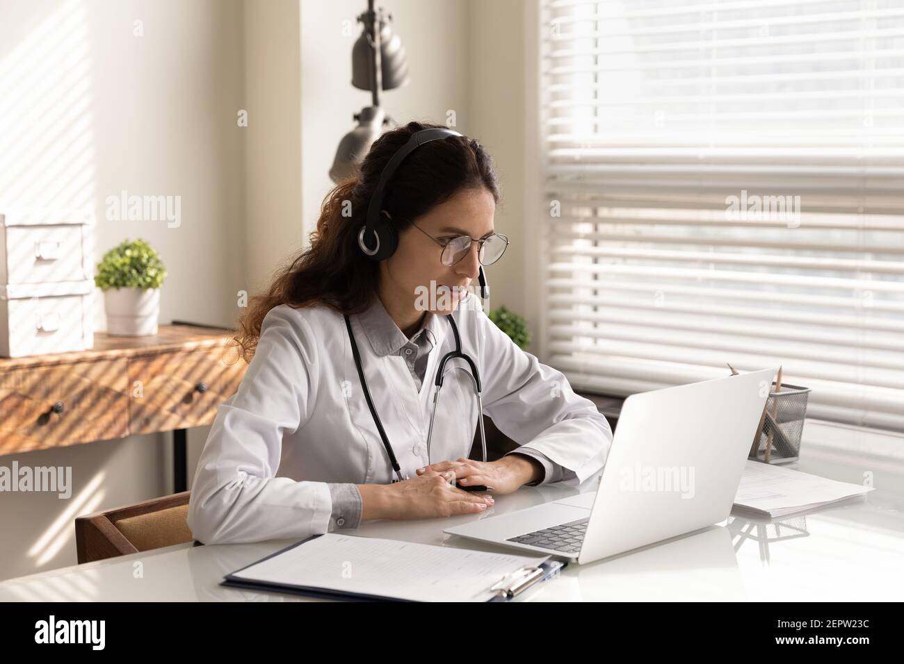 Professional female doctor wearing headphones consulting patient online ...