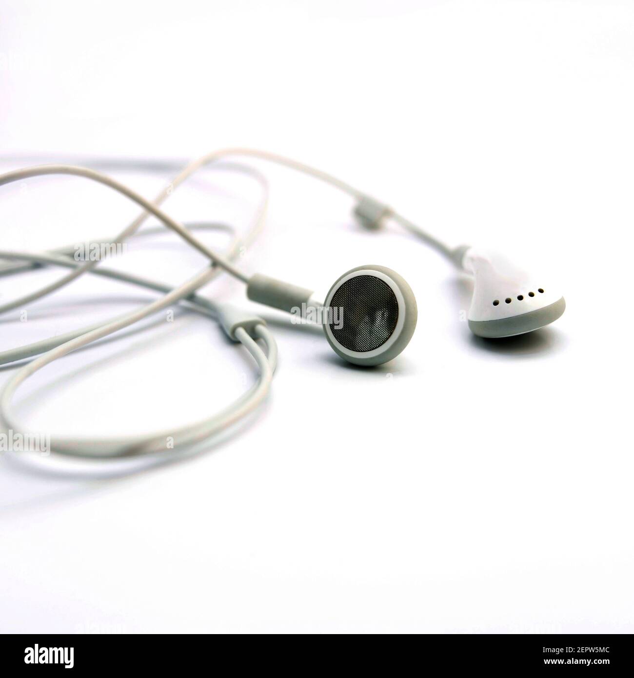 Close-up of white earbuds with tangled cord on a plain background ...