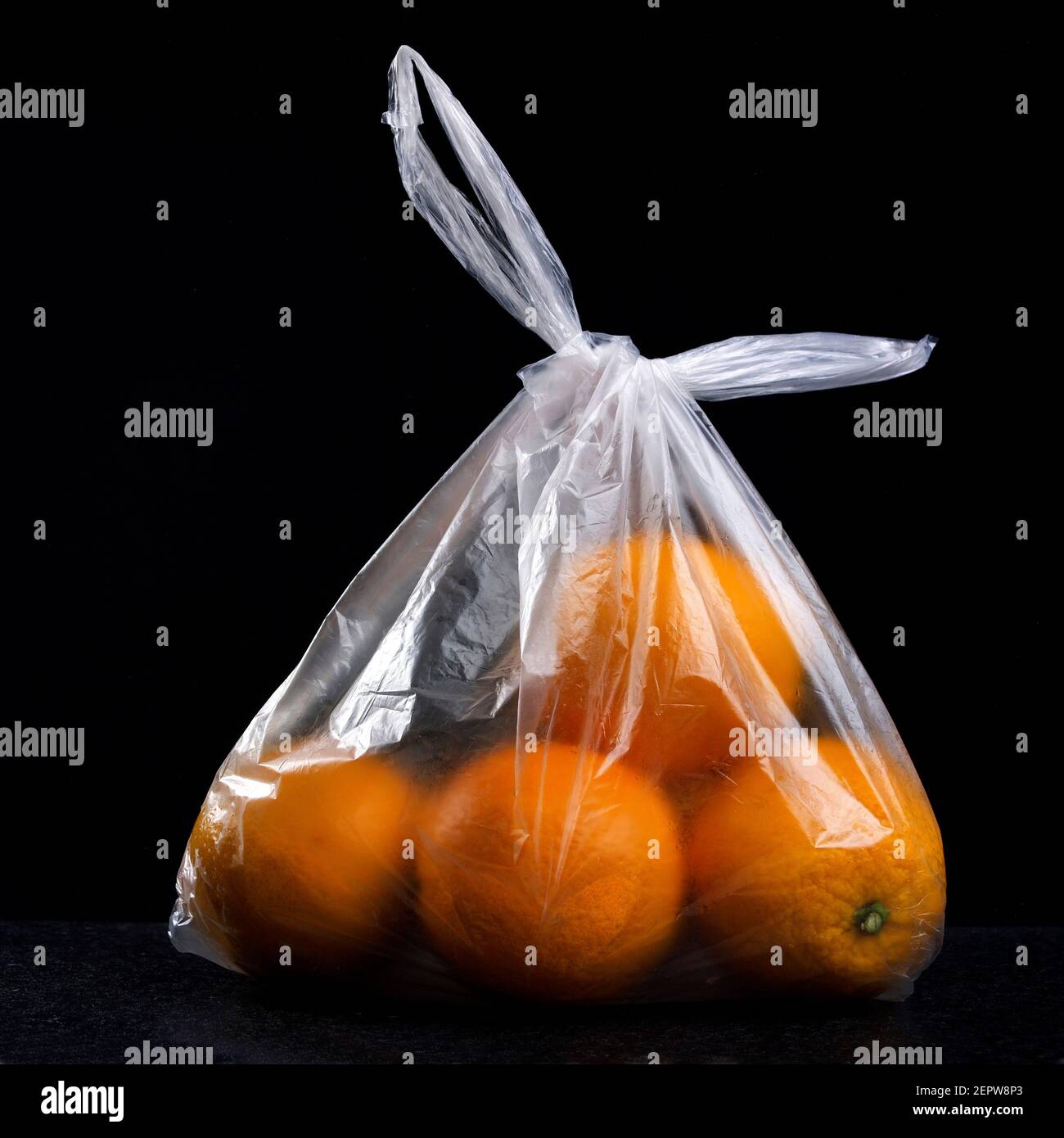 A transparent plastic bag filled with fresh oranges against a dark ...
