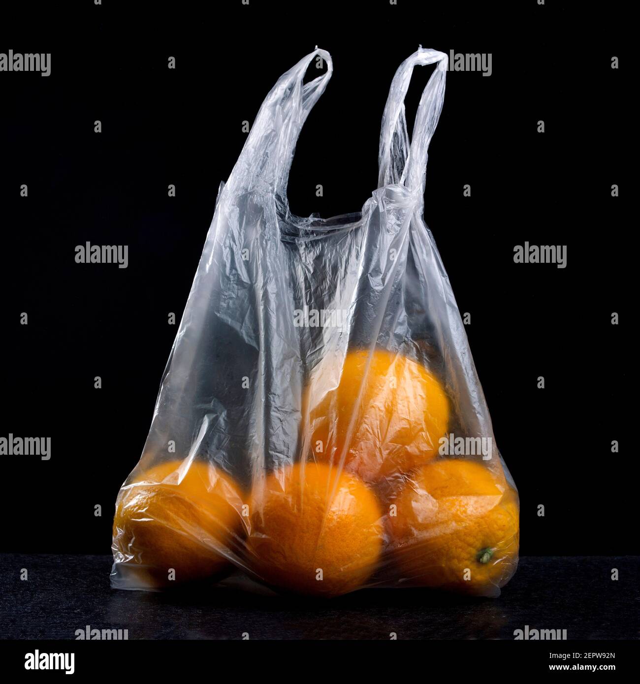 A transparent bag containing fresh oranges on a solid black background ...