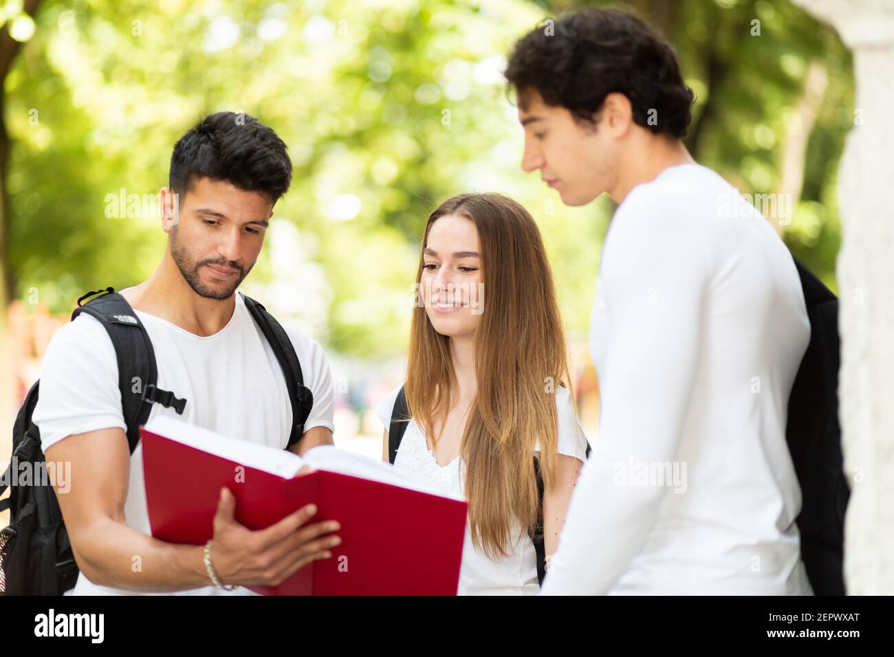 Three students talking to each other outdoor in a college courtyard ...