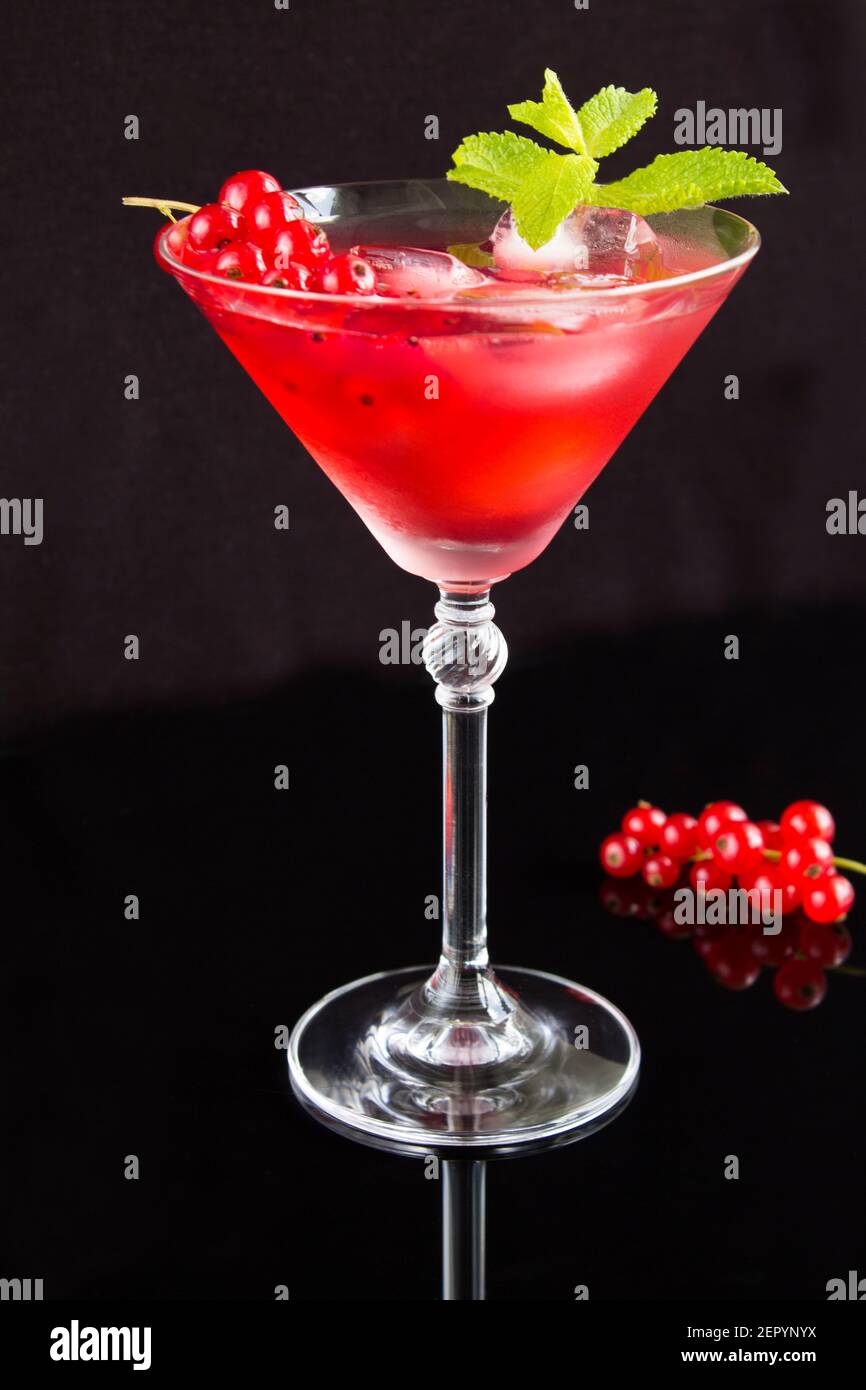 Cold cocktail with red currants in the martini glass on the dark ...