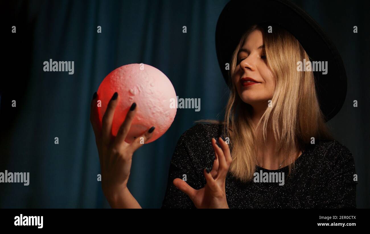 A young woman fortune teller in a hat is holding a magic ball ...