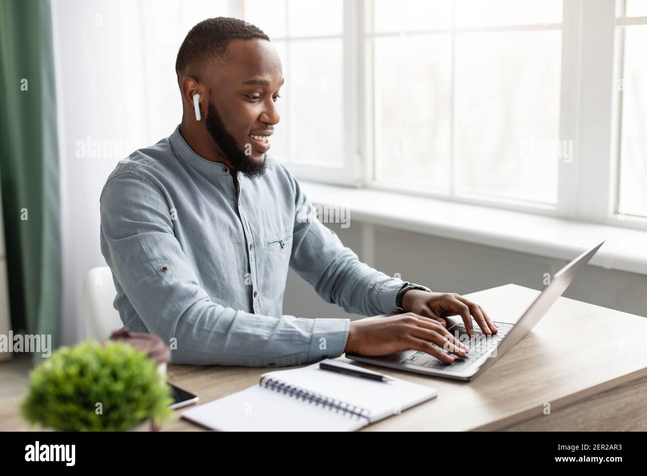 Black Businessman Working On Laptop Wearing Earbuds In Modern Office ...
