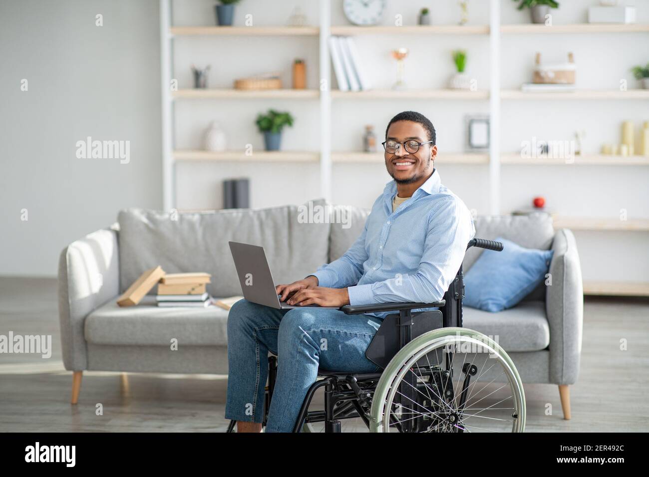 Happy disabled black man in wheelchair using laptop, working online ...
