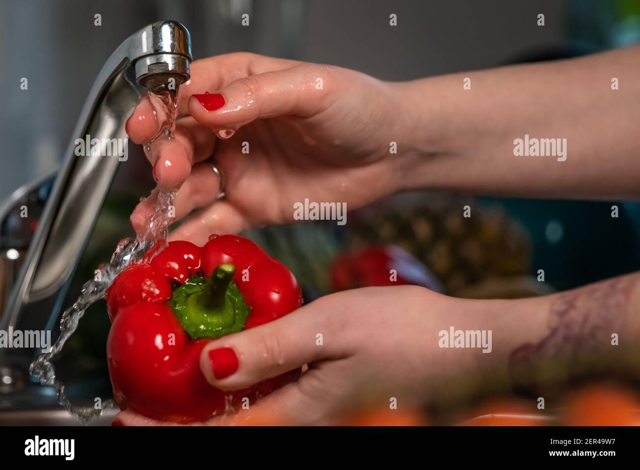 Close up woman's hands washing homegrown red organic paprika with the ...