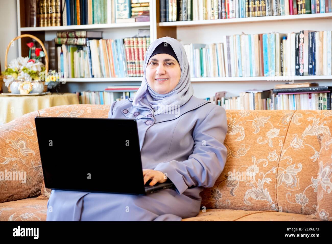 Happy arabic muslim woman sitting on couch alone using technology Stock ...