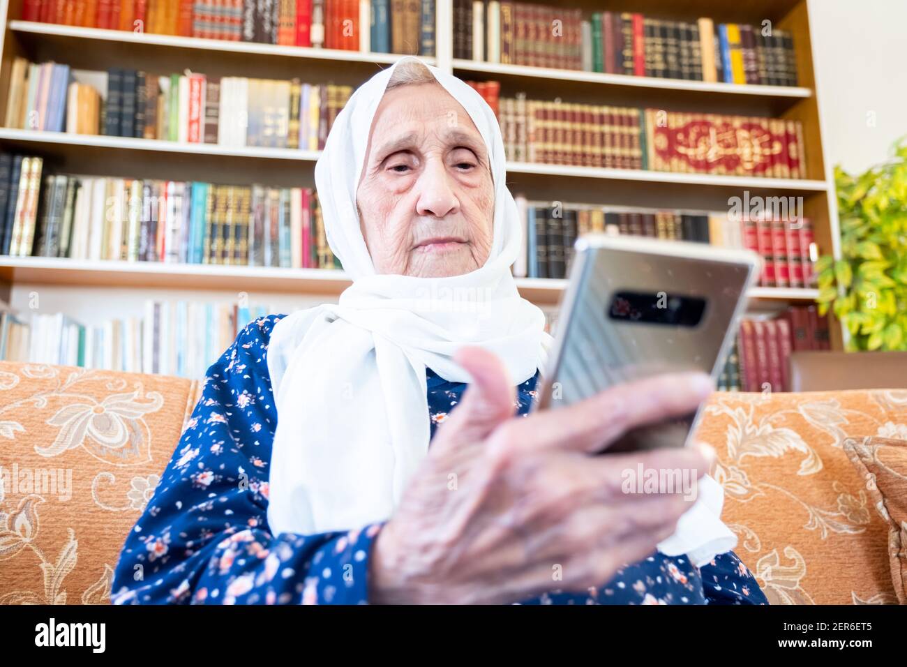 Happy old arabic muslim woamn using technology while sitting on couch ...