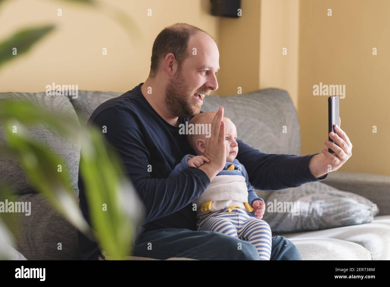Happy father and son taking selfie with smartphone sitting on the couch ...