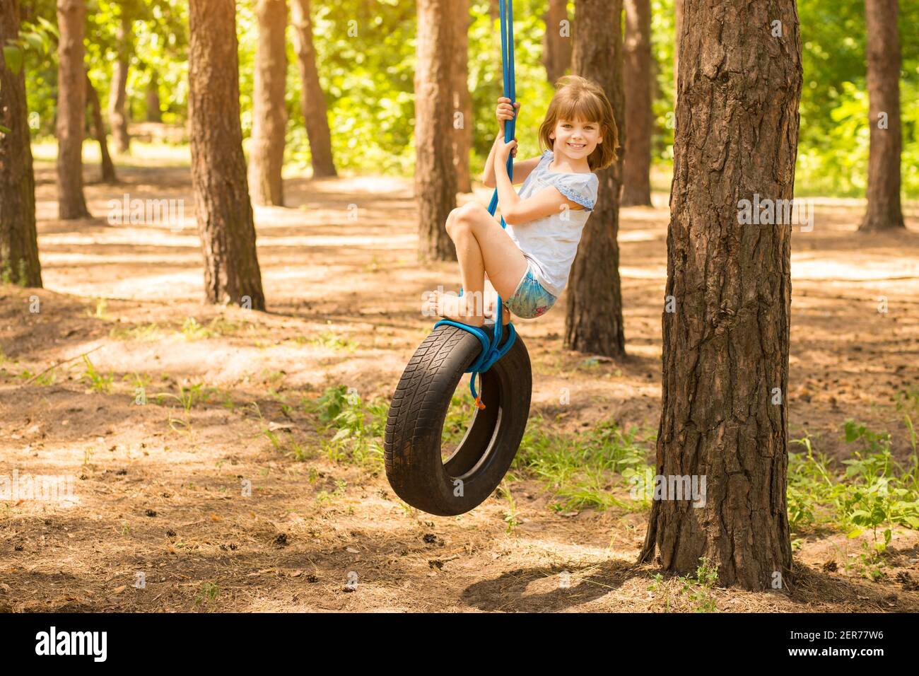 Cute little girl swinging on wheel attached to big tree in autumn ...