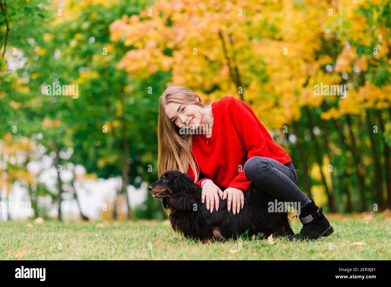 Woman hugging dog in the summer park. Cheerful lady with long dark hair ...