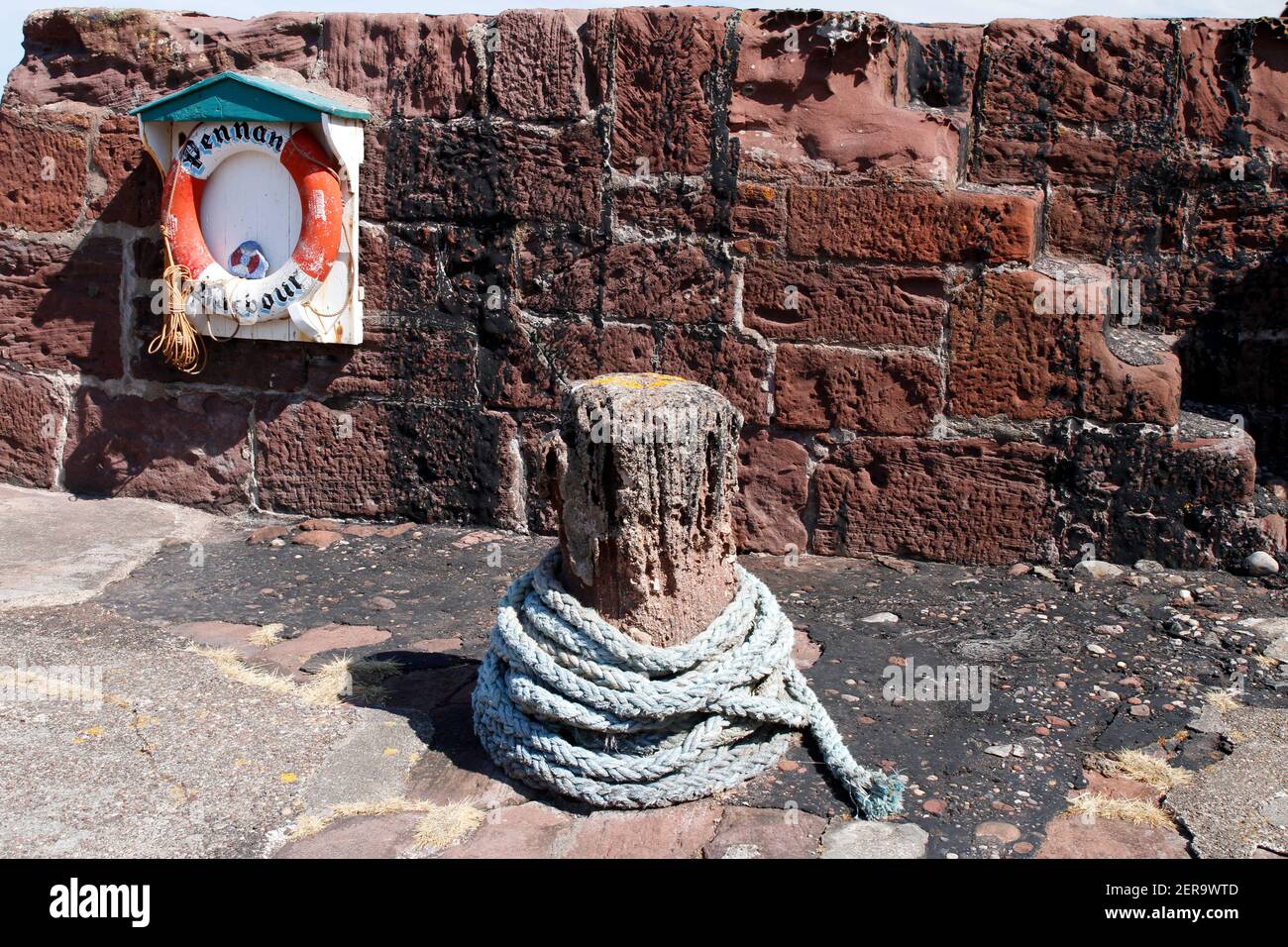 Worn stone bollard on the quay and lifebuoy on harbour wall, Pennan ...