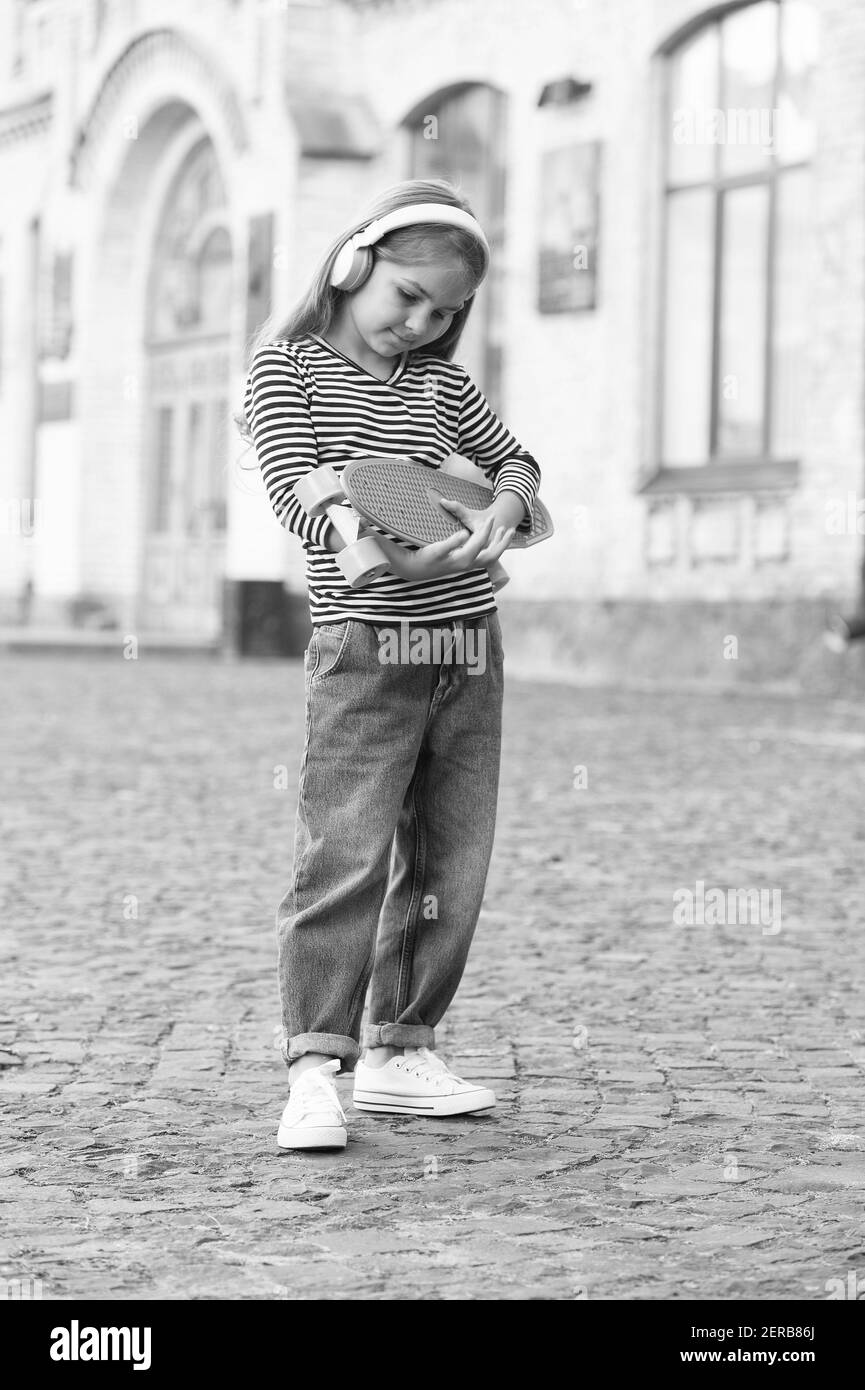 Small kid hold penny board and listen to music in headphones outdoors ...