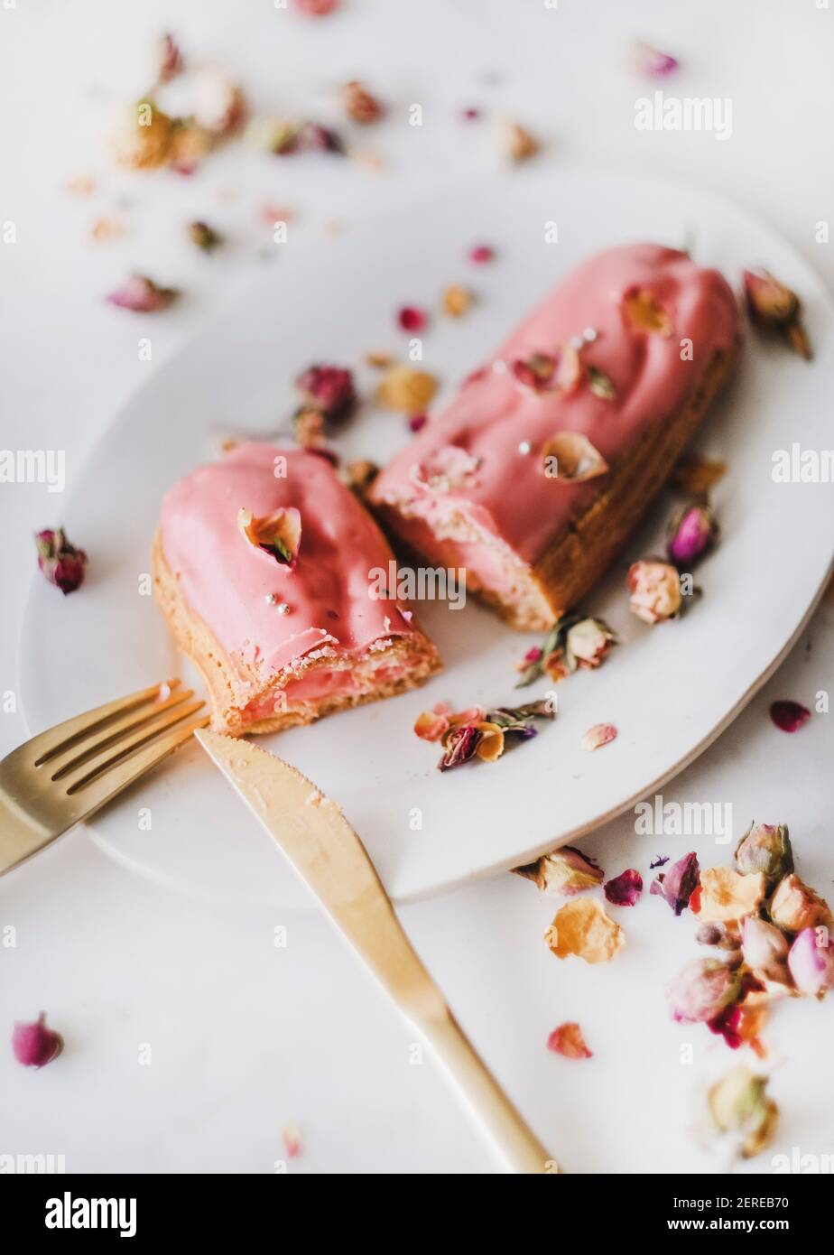 Rose eclair dessert with dried rose petals on white oval plate with ...