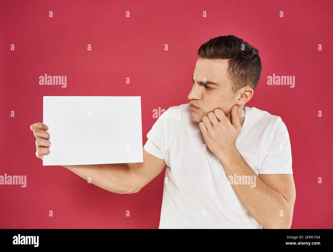 Puzzled young man on a red background are looking at a flyer in hand ...