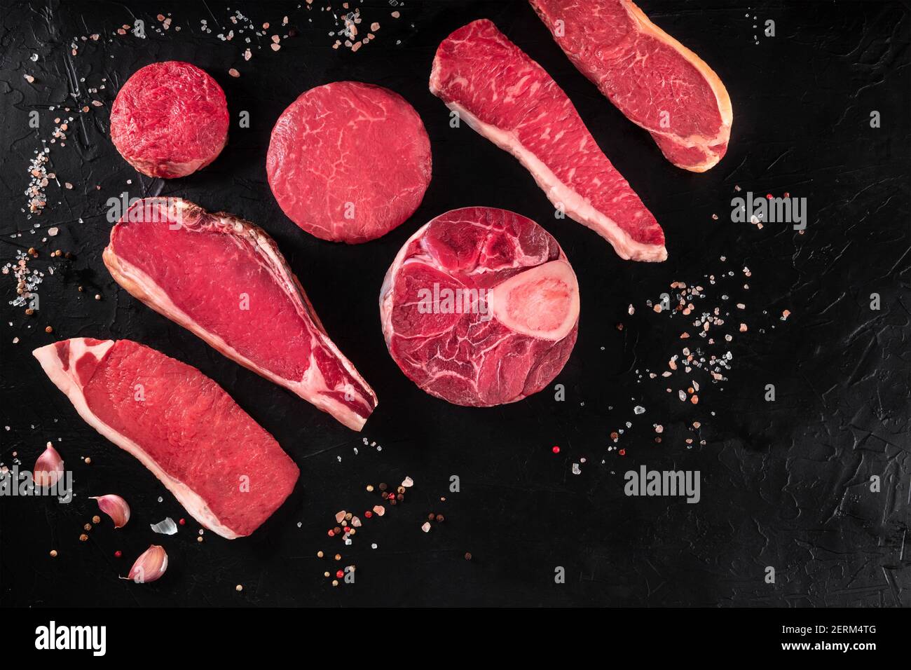 Raw meat cuts with salt and garlic, overhead flat lay shot on a dark ...