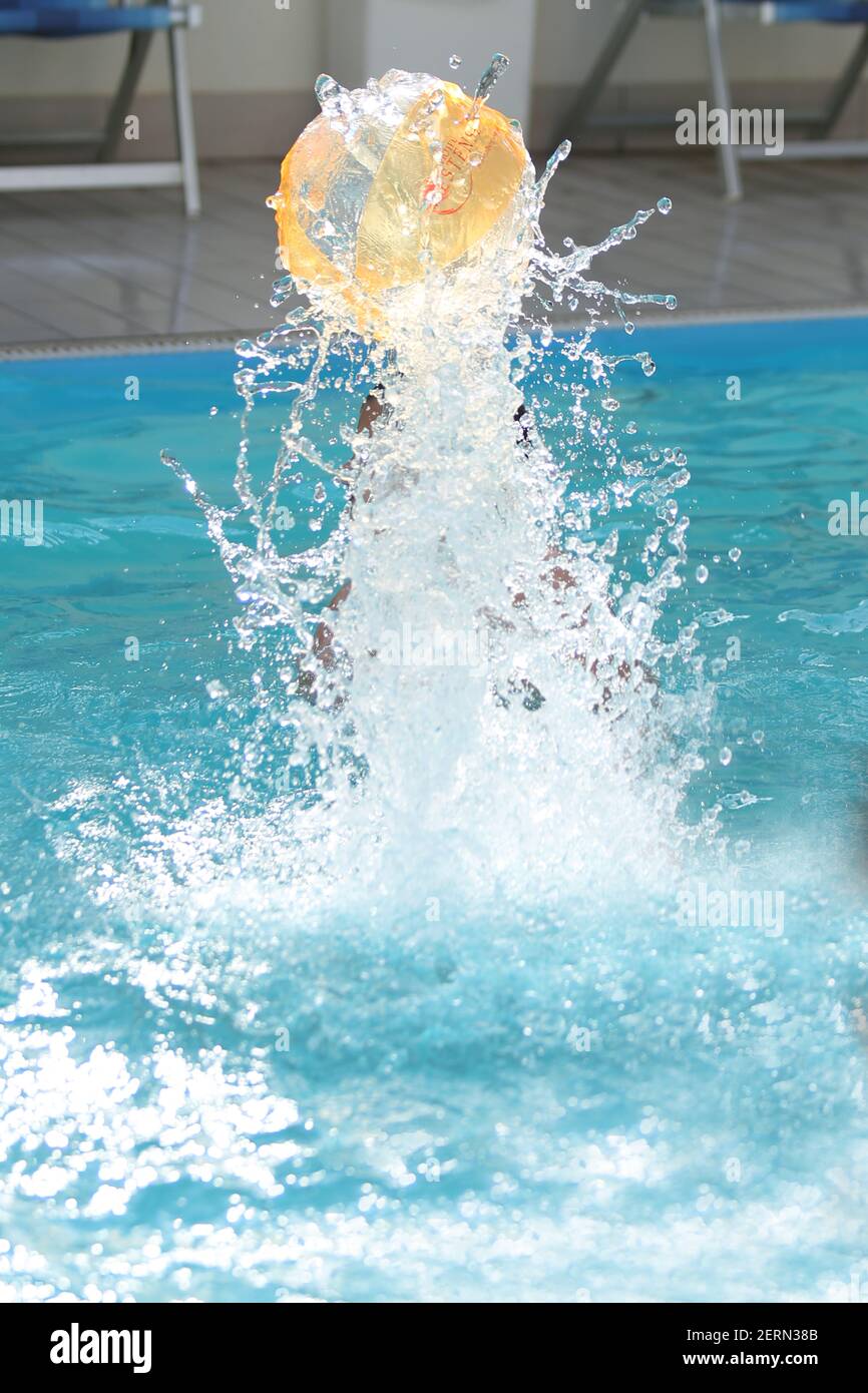 A vertical shot of water splashes in the swimming pool with a ball ...