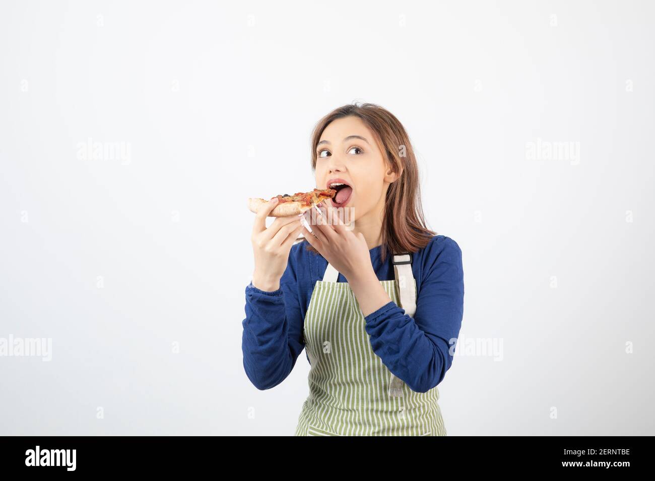 Portrait of young woman in apron eating pizza on white background Stock ...