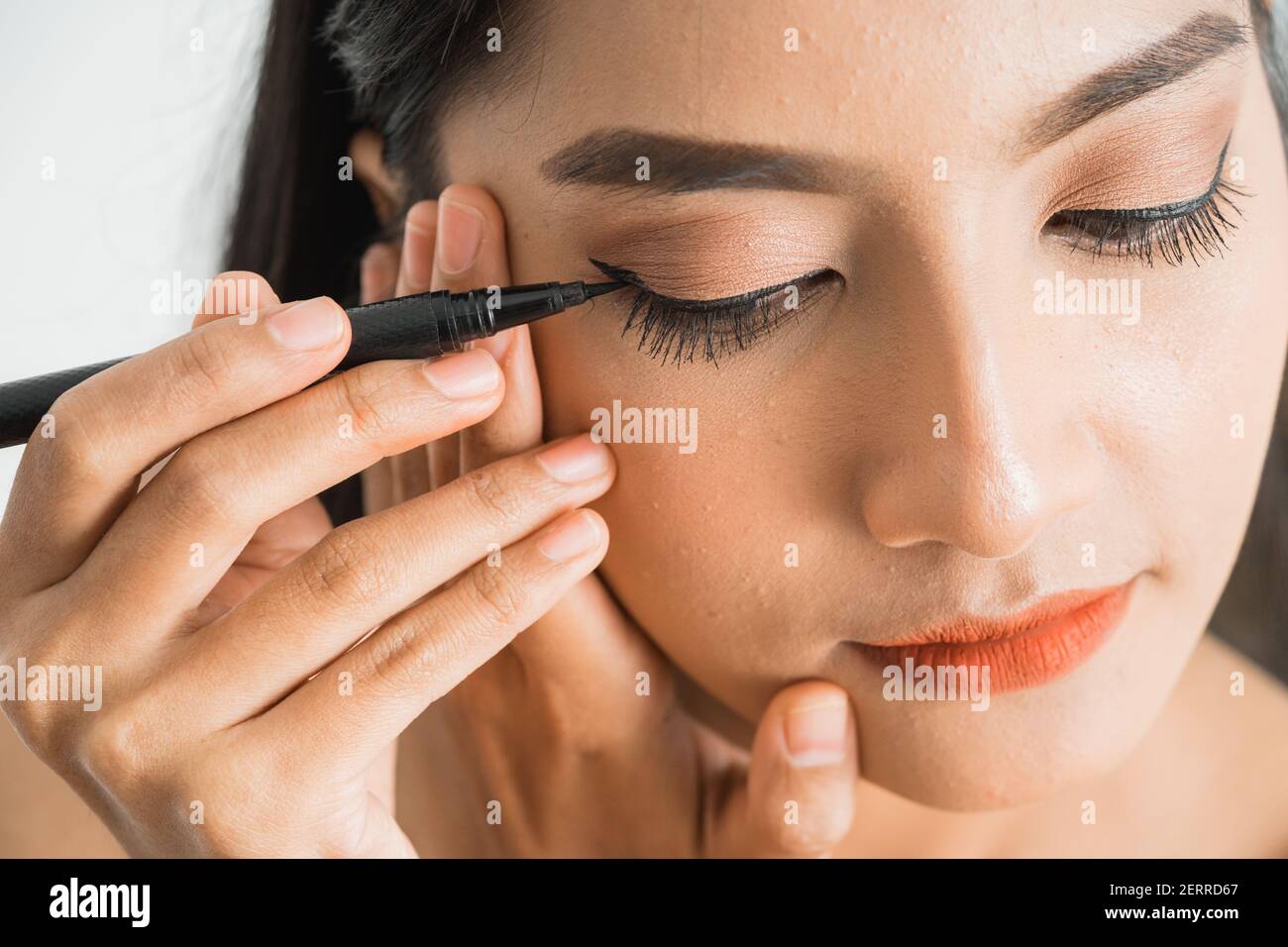 Mixed Race Asian Woman Putting Eye Liner On Eyelid On White Background