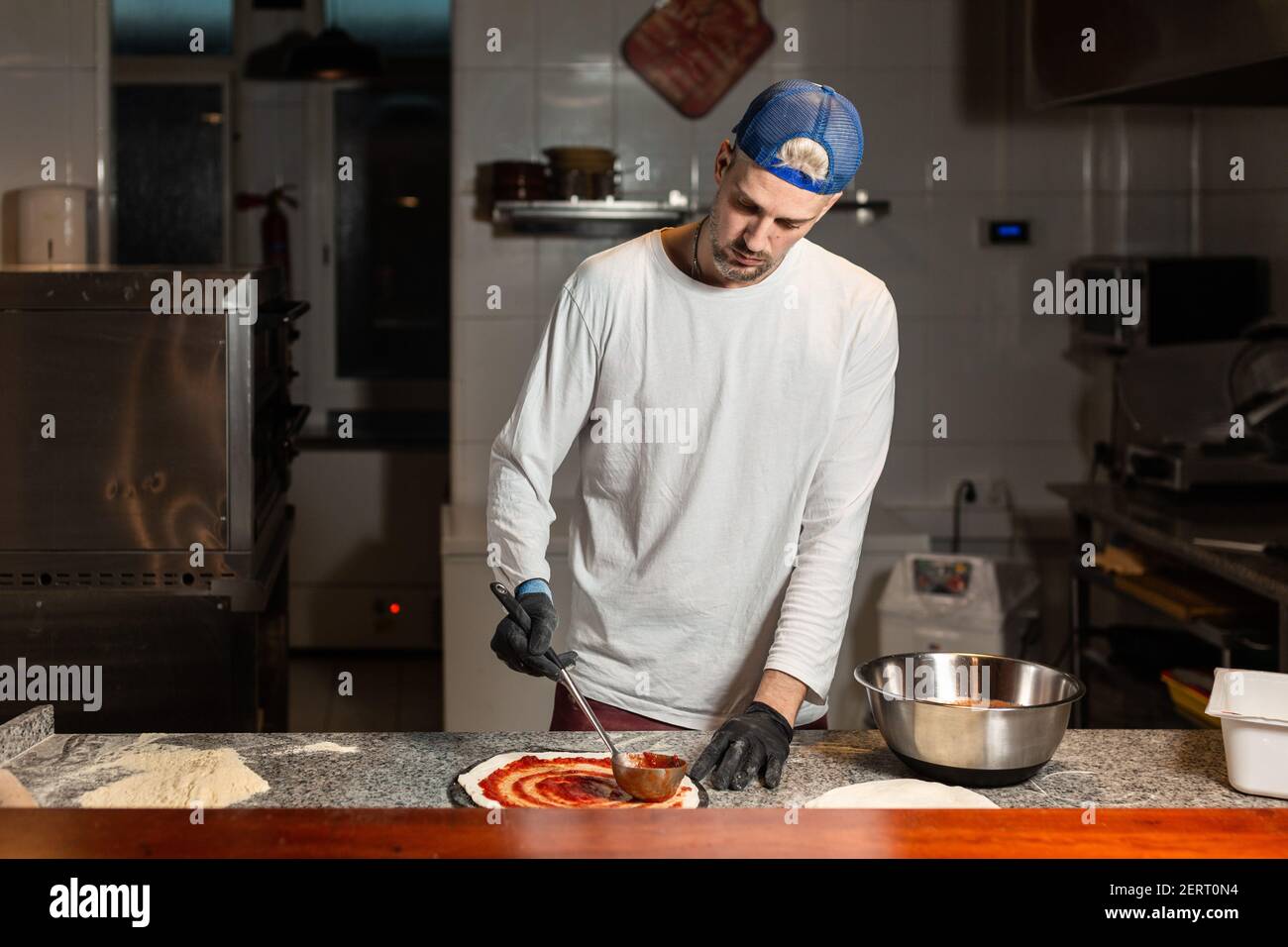pizza man adds tomato to a pizza in a pizzeria restaurant kitchen Stock ...