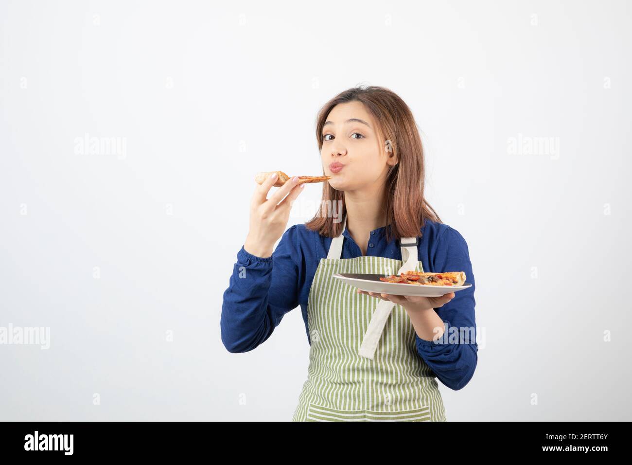 Portrait of young girl in apron eating pizza on white background Stock ...